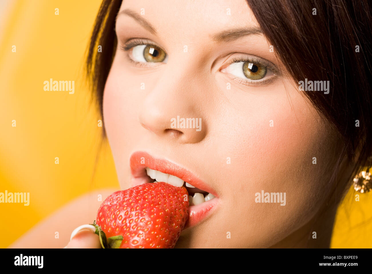 Horizontal image of pretty woman eating strawberry on orange background ...