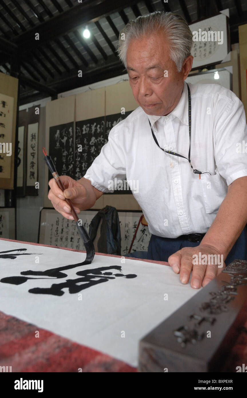 A man doing Traditional Chinese writing in ink using a brush on paper ...