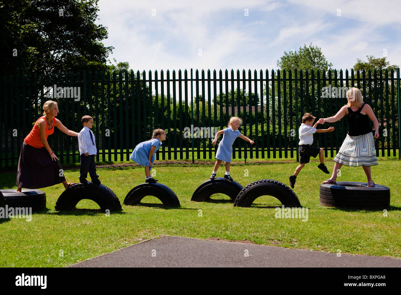 two teachers help guide primary school pupils over a playground ...