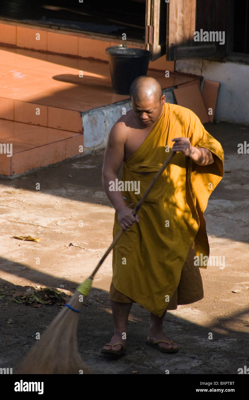 A Buddhist monk is sweeping a courtyard with a broom on temple grounds ...