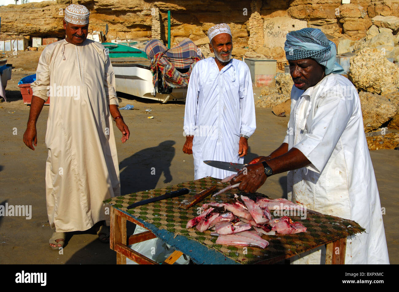 Fishmonger cutting fish for two Arab clients at an open-air market ...