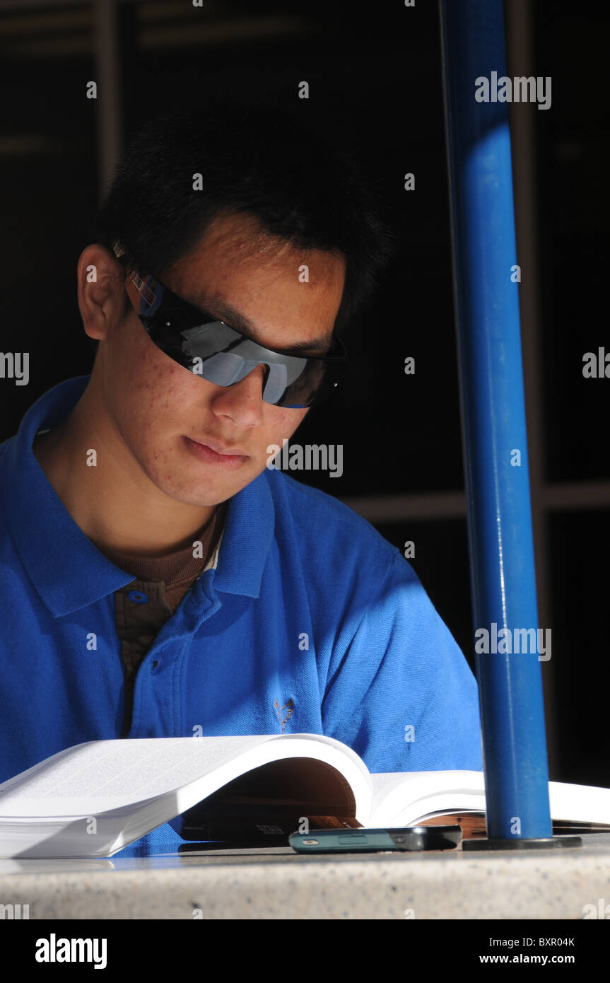 A college student studying outdoors sits in the shade and wears eye ...