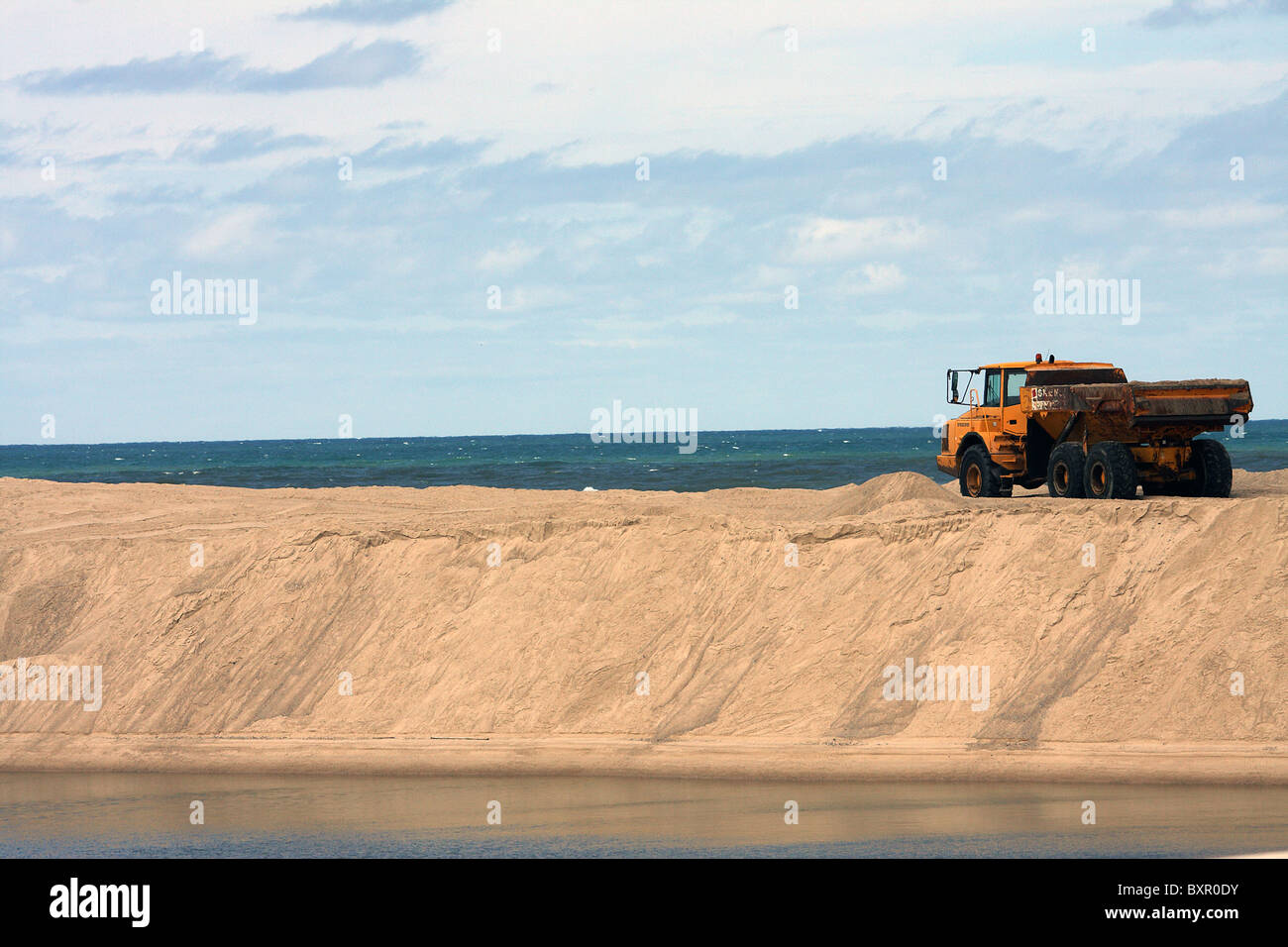 A dumper truck on the sandy beach at the seaside moving sand by the sea ...