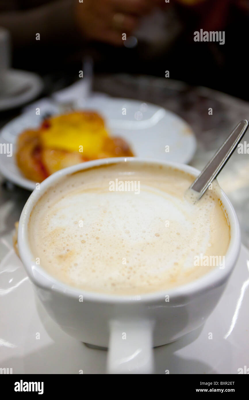 Close-up of a frothy cappuccino in a white cup with a blurred pastry in ...