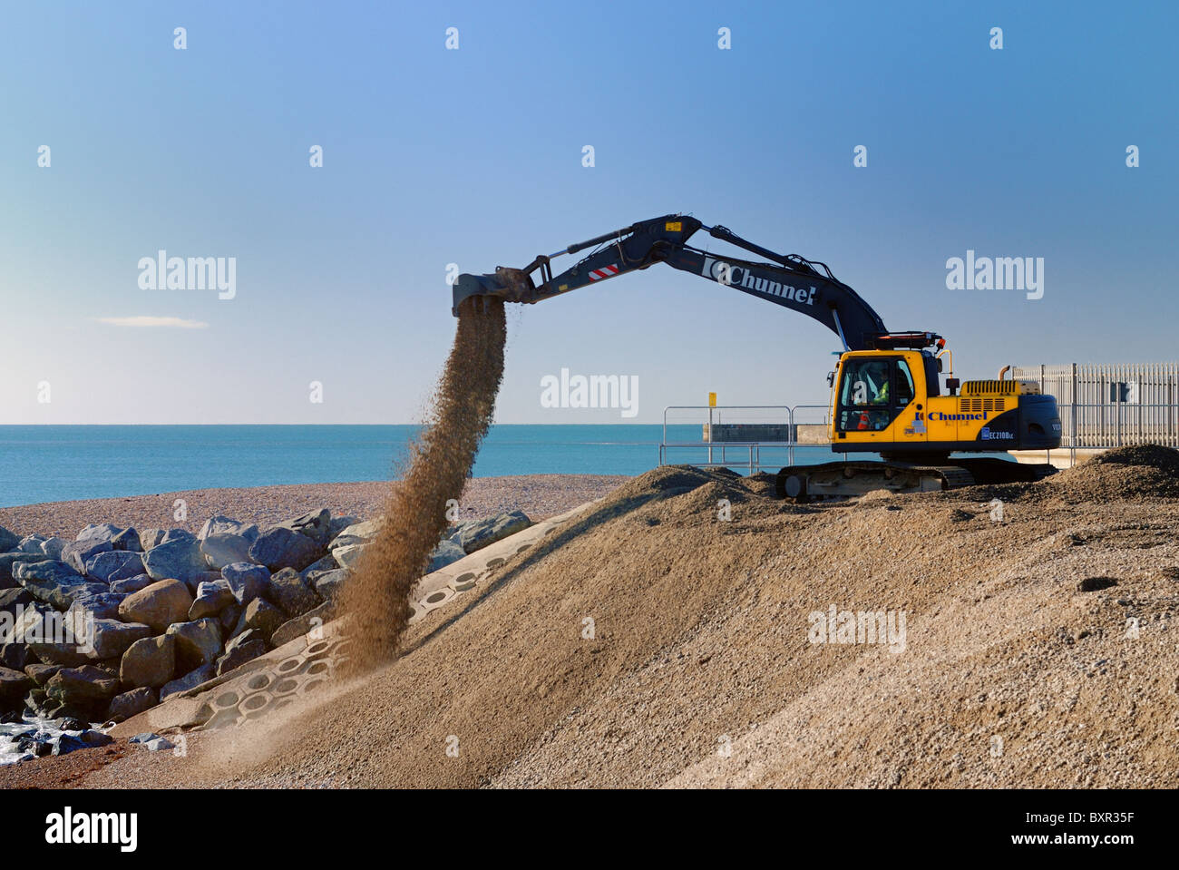 A large digger reinforcing sea defences following beach erosion Stock ...
