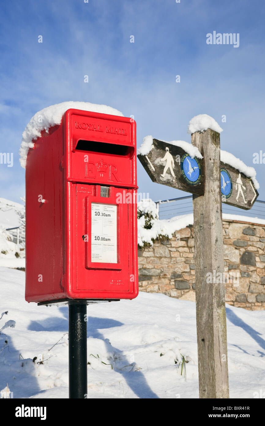 Traditional British red postbox and coastal path signpost in the snow ...