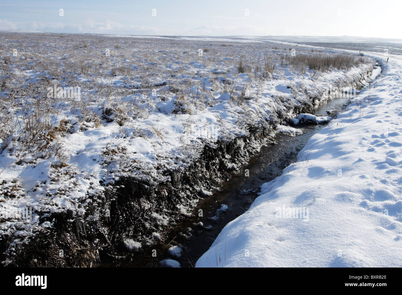 Drainage ditch at edge of heather moor running alongside a road with ...