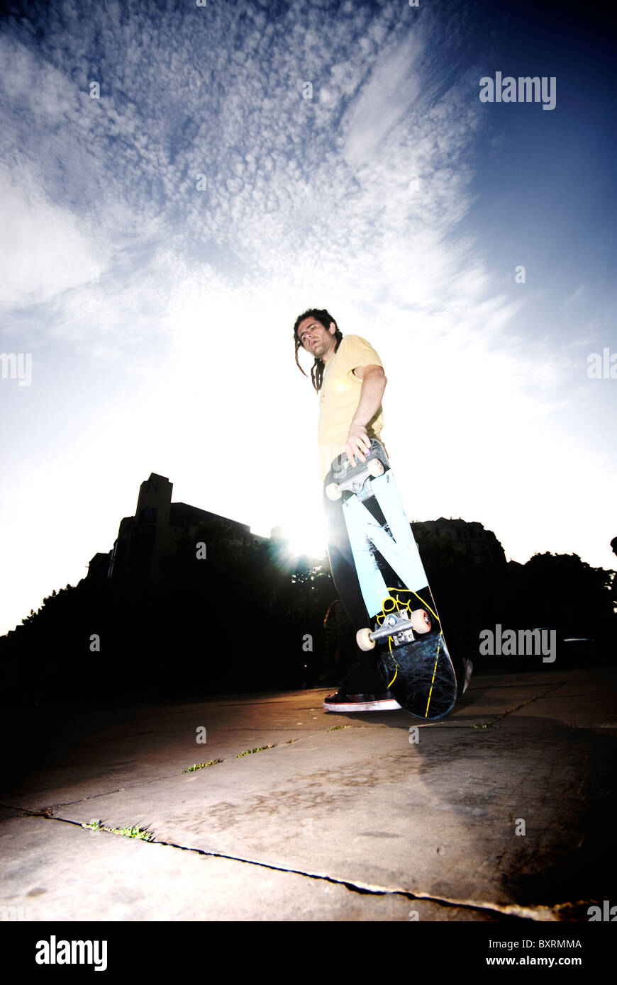 young and strong skateboarder stand up with hard backlight and blue sky ...