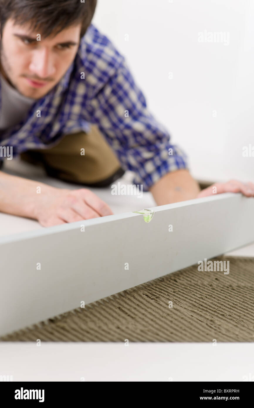 Home tile improvement - handyman with level laying down tile floor ...
