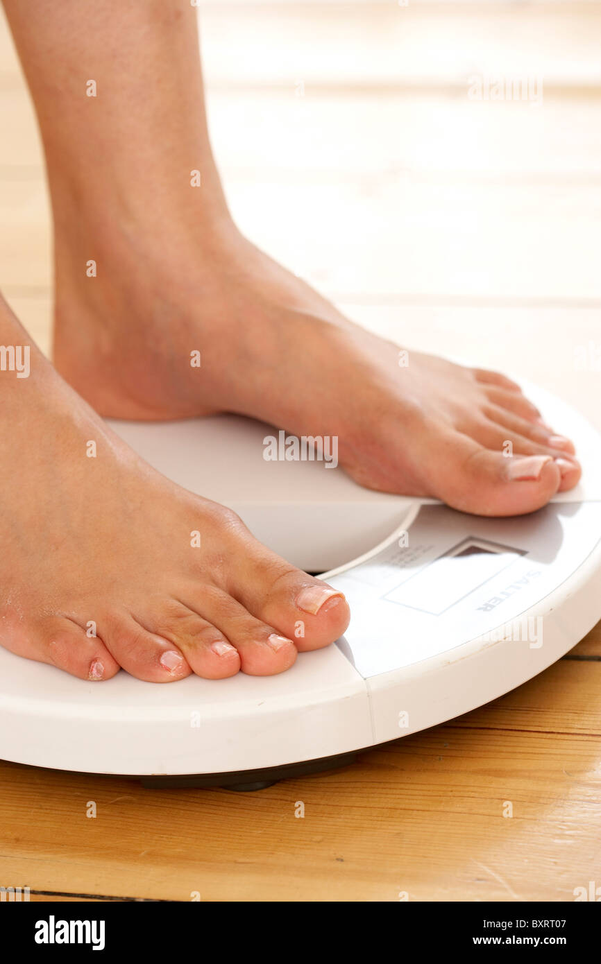 Woman's feet standing on weighing scales Stock Photo - Alamy