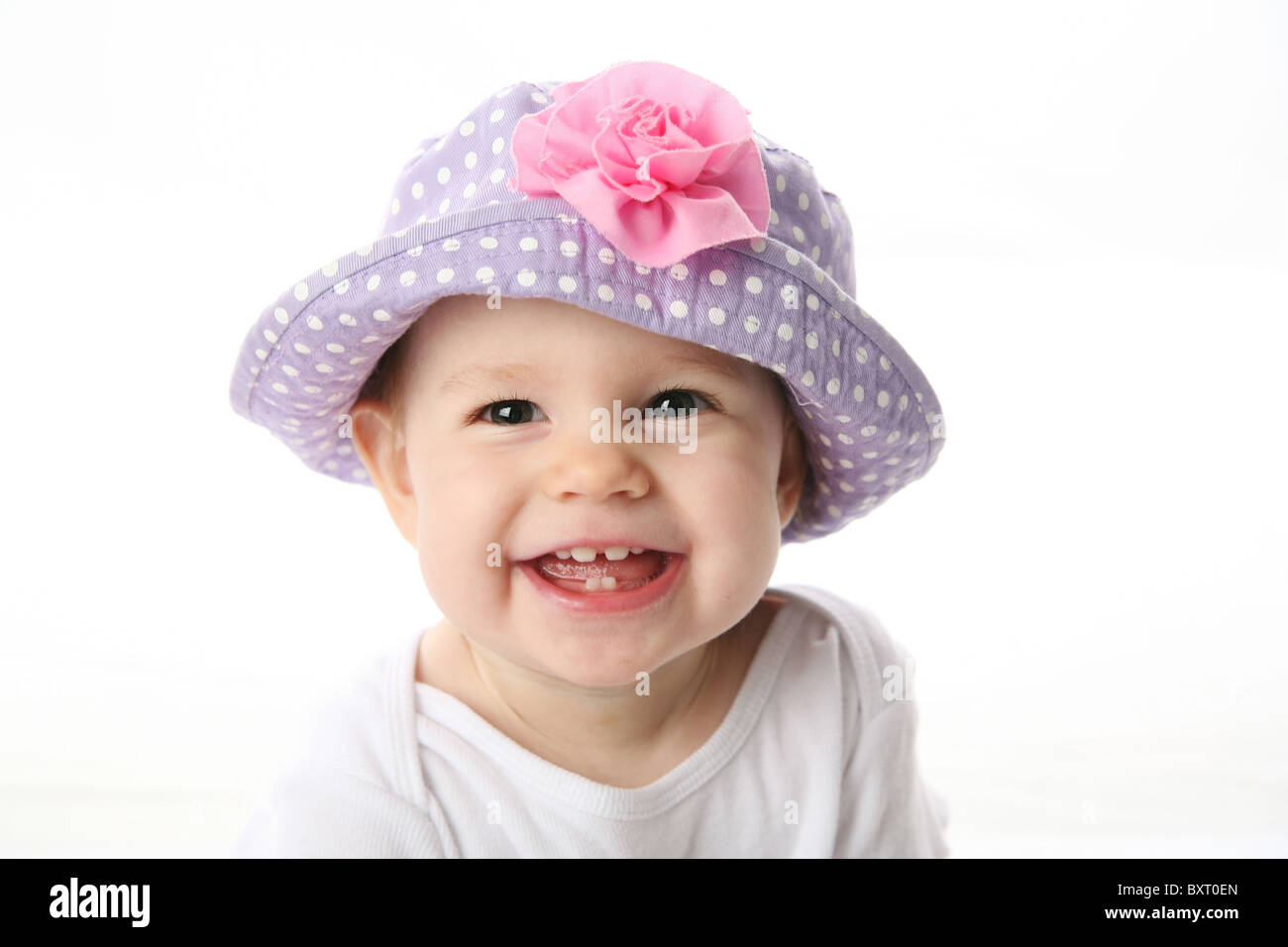Smiling baby girl showing teeth wearing a purple polka dot hat with ...