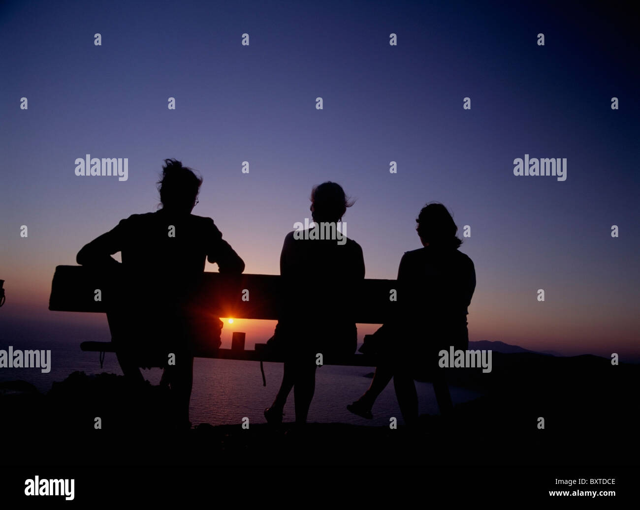 Three Women Watching The Sun Set Over Coastline Stock Photo - Alamy