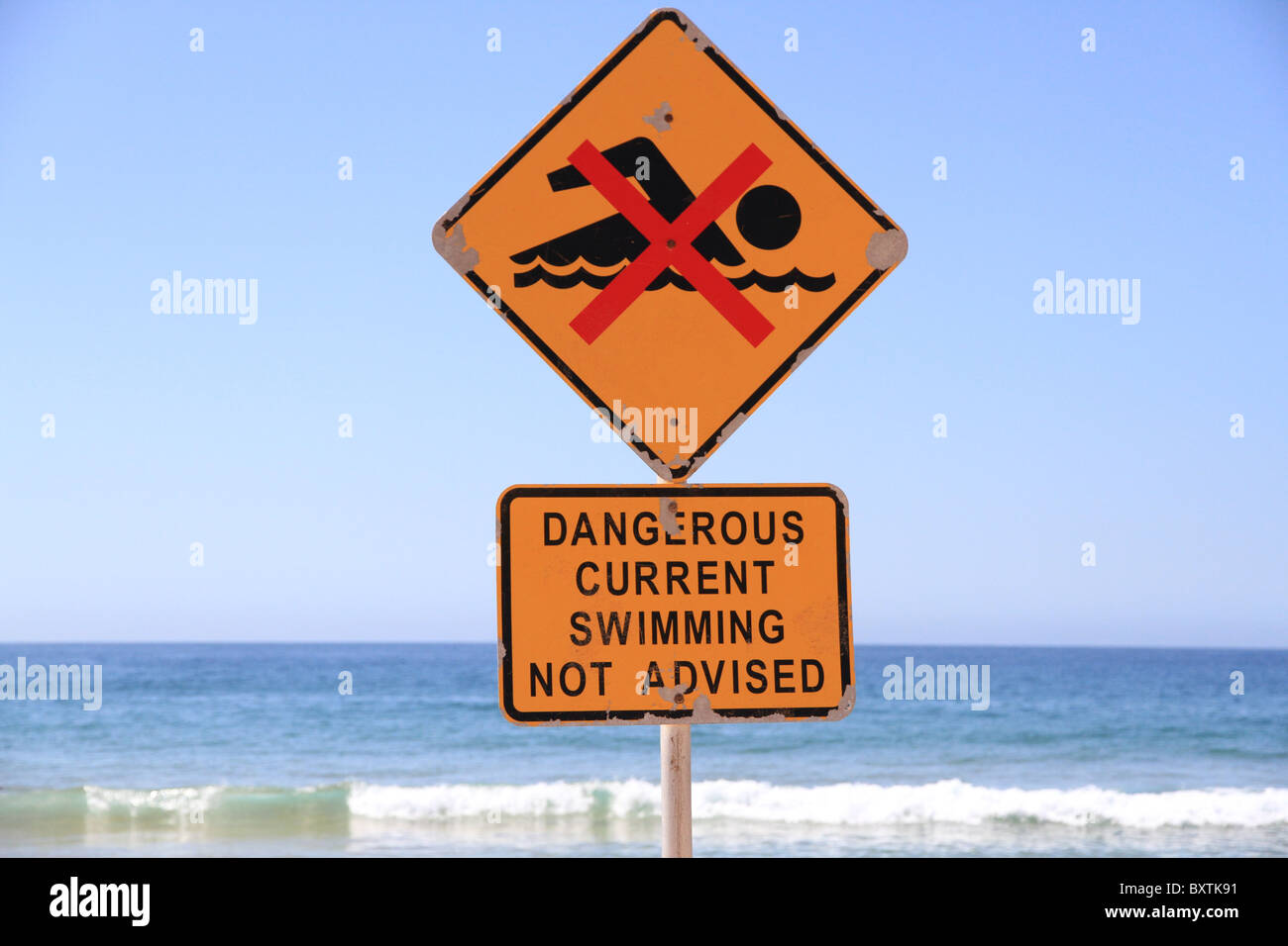 A yellow sign against a blue sky and surf background warning of ...