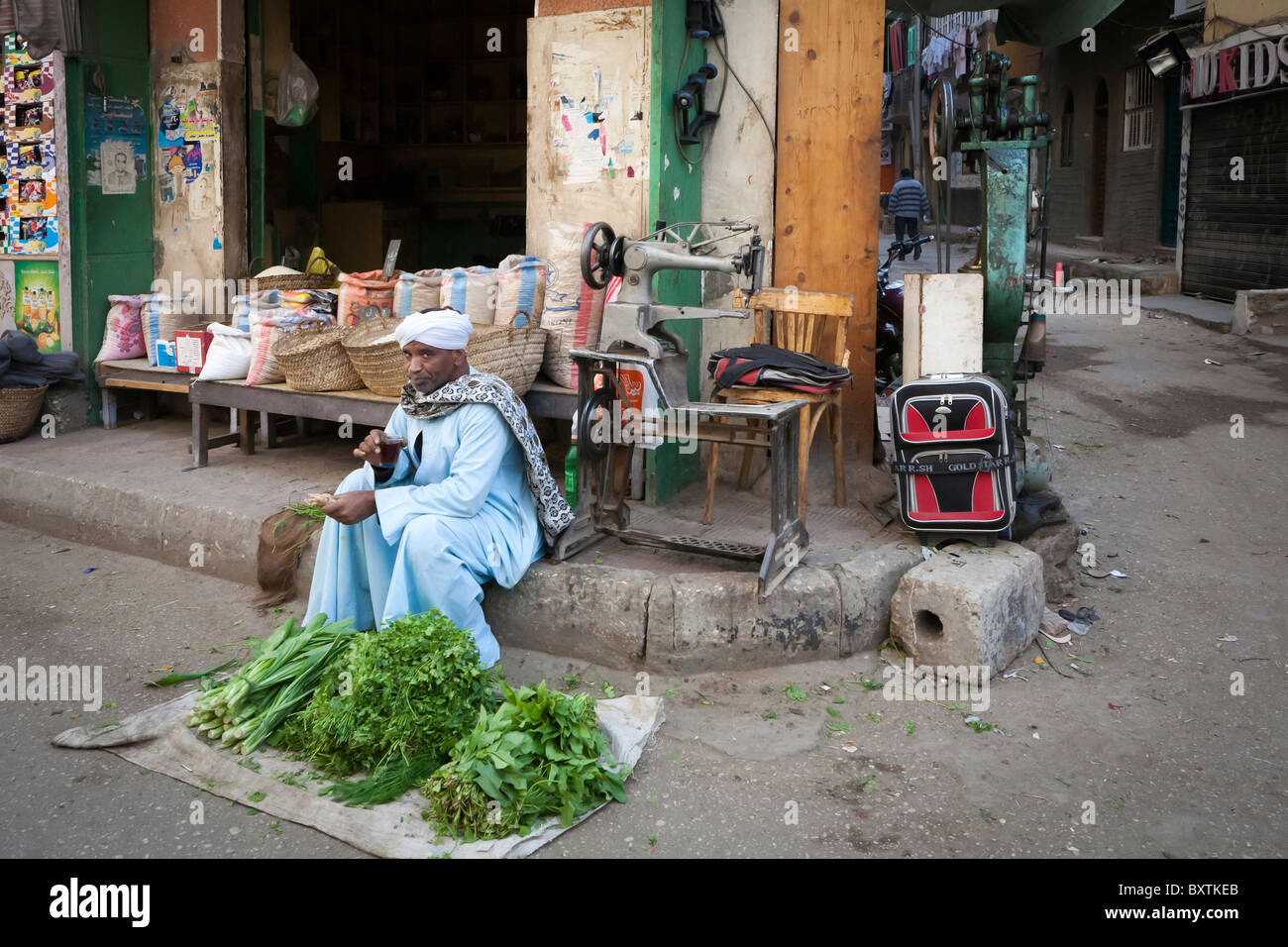 Herb seller sitting on pavement drinking tea at a local street market ...