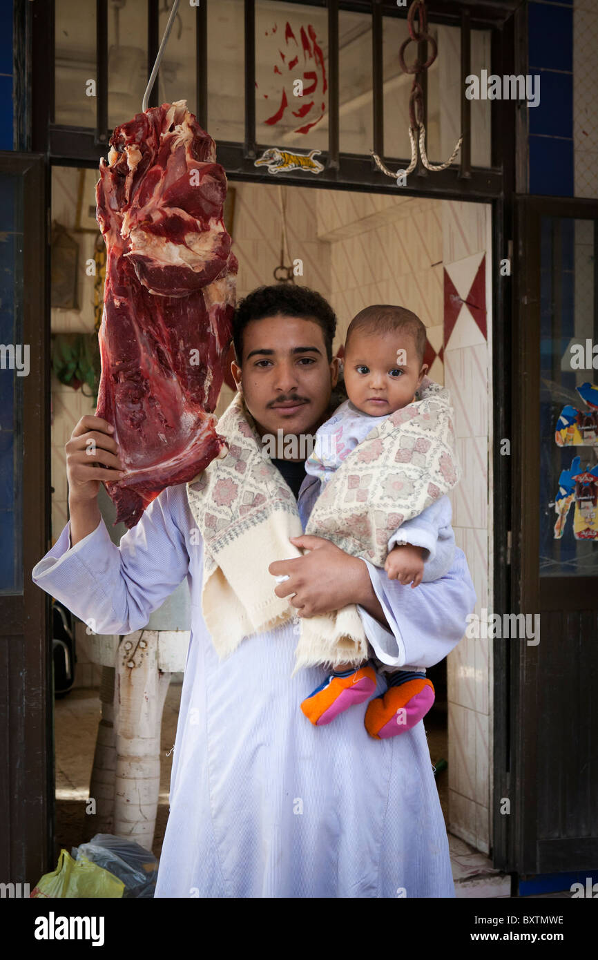 Young butcher proudly holding infant child and meat carcase outside his ...