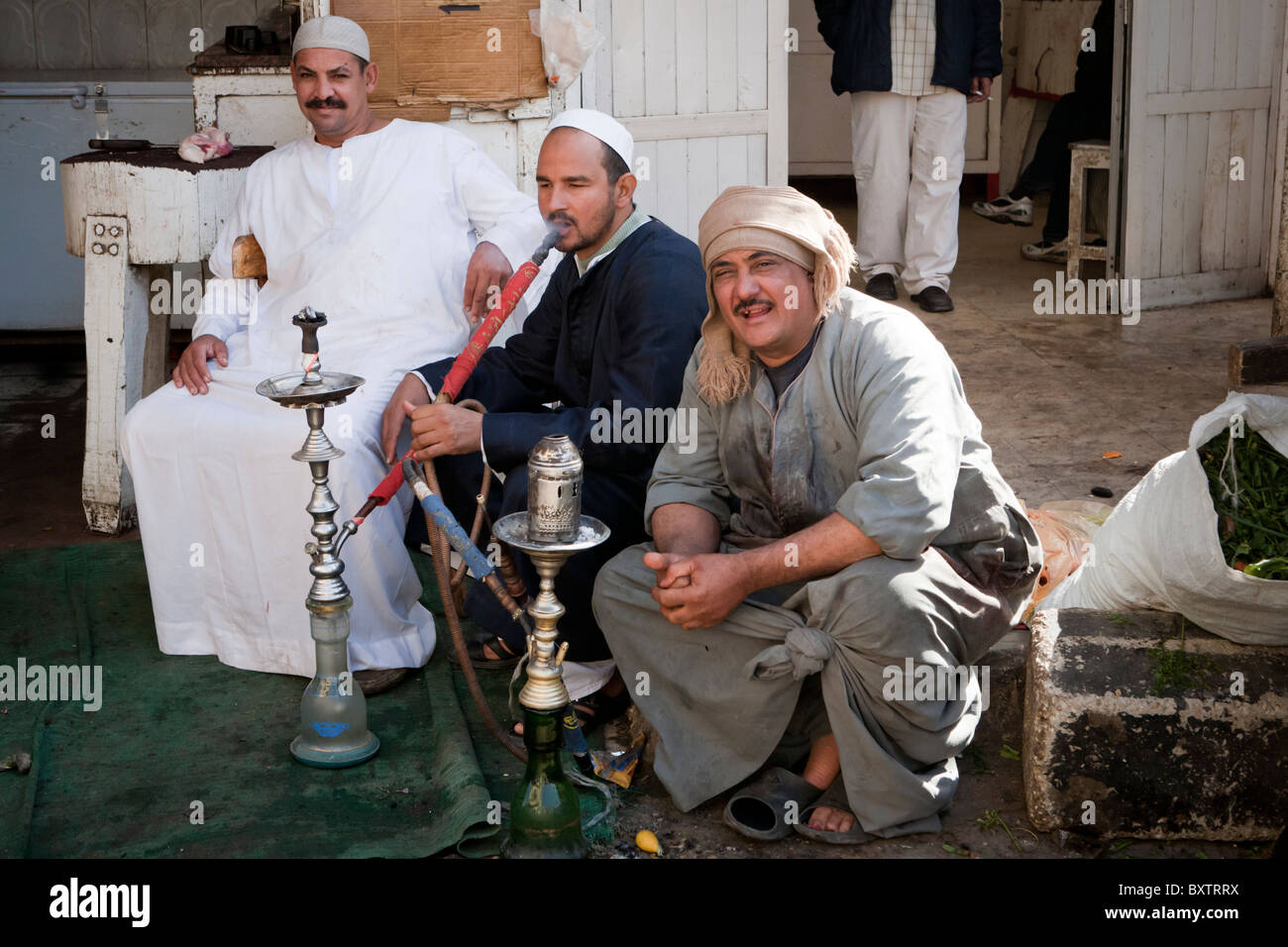 Three butchers resting outside their shop, one smoking a shisha, at a ...