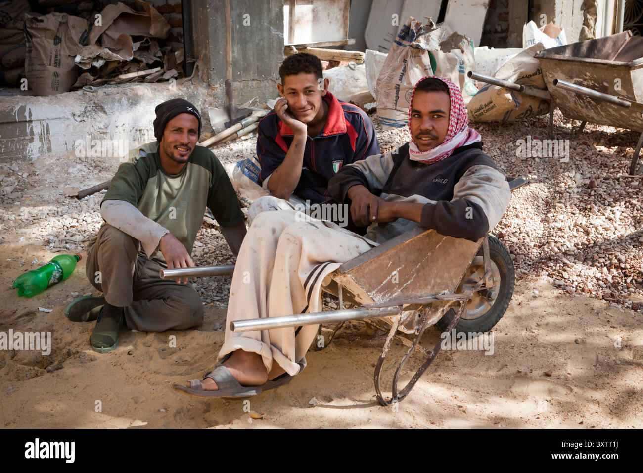Builders relaxing at work, one sitting in a wheel barrow, at a local ...
