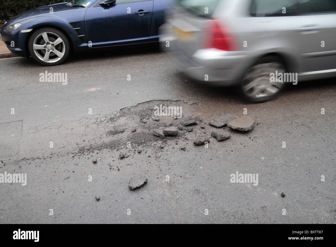 Car passing a new pot hole, with broken tarmac, the result of the heavy ...