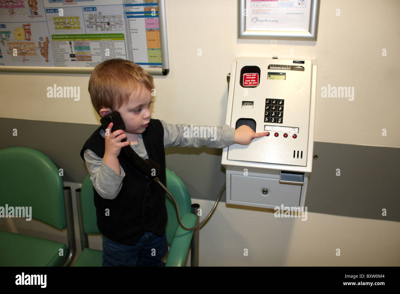 A young boy using a public payphone to telephone people in the hospital ...