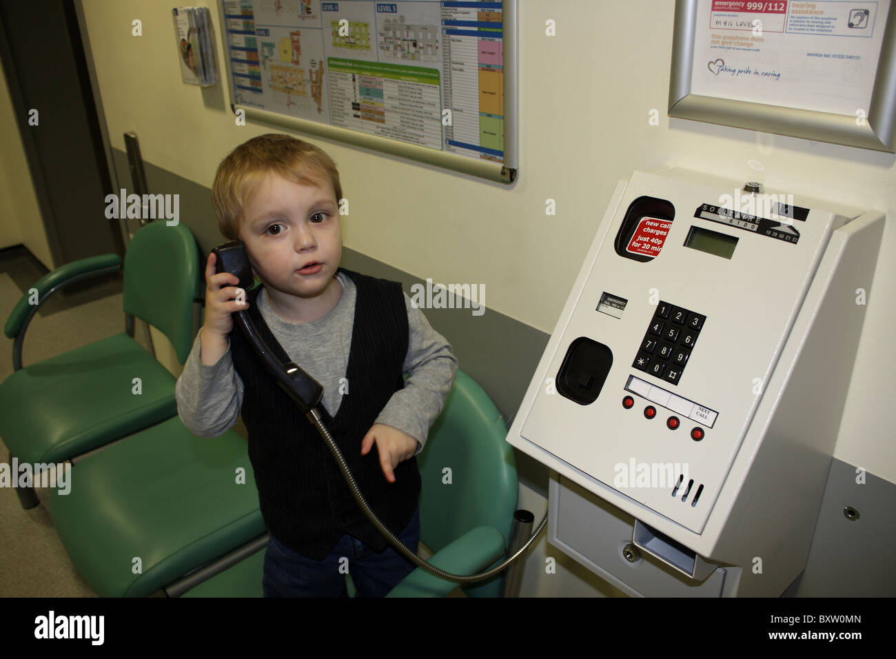 A young boy using a public payphone to telephone people in the hospital ...