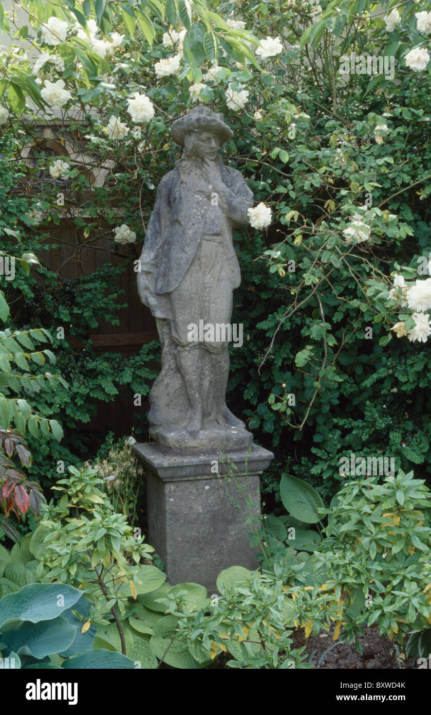 Stone statue surrounded by white roses in country garden in summer ...