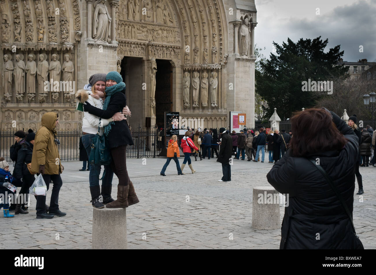 Two young women standing on a bollard hugging whilst having their ...
