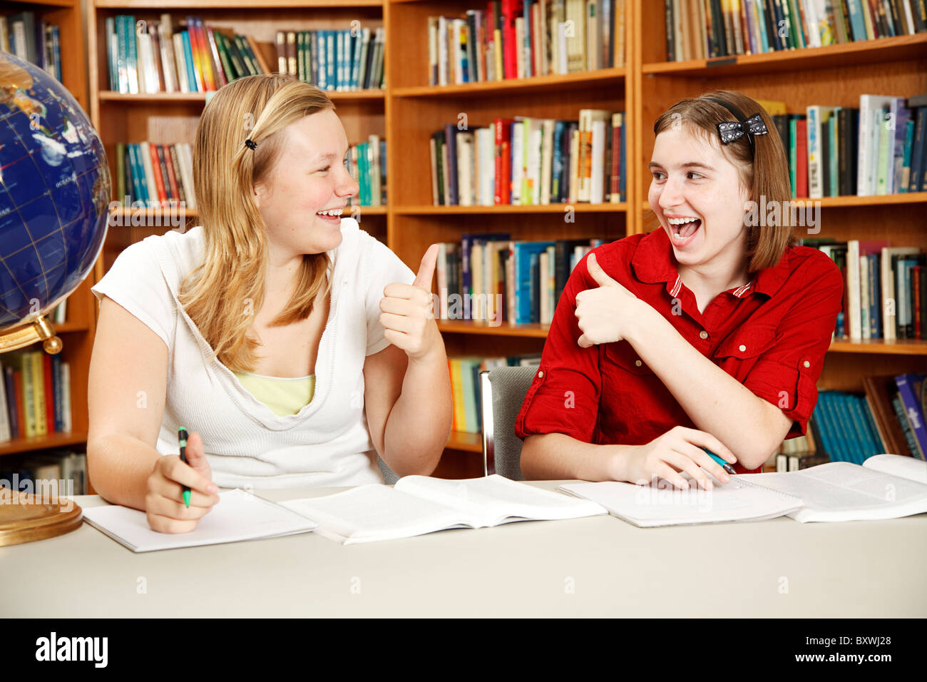 Teen girls doing their homework in the school library and giving each ...