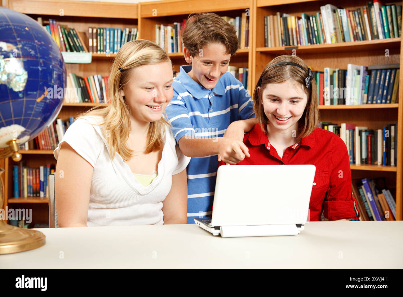 Two teen girls and a younger boy using a netbook computer in the school ...