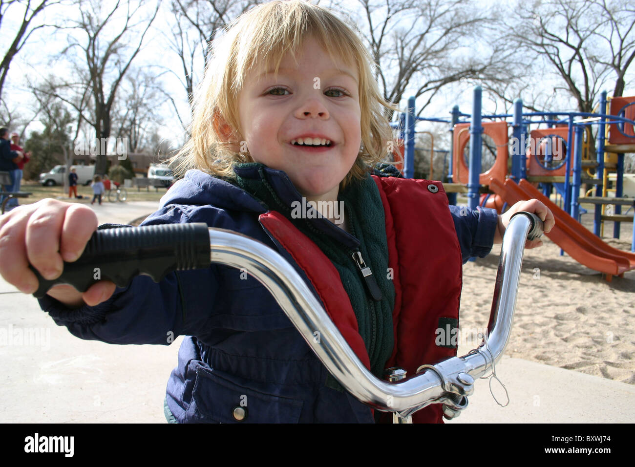 Two year old boy proudly riding a bicycle, holding large handle bars at ...