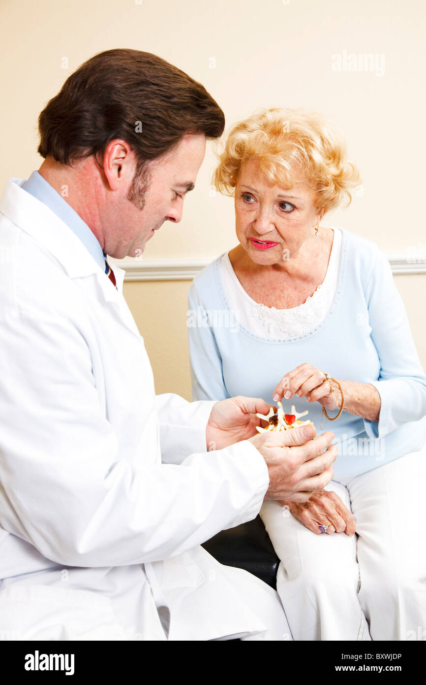Chiropractor shows senior patient a model of the spine and discusses ...