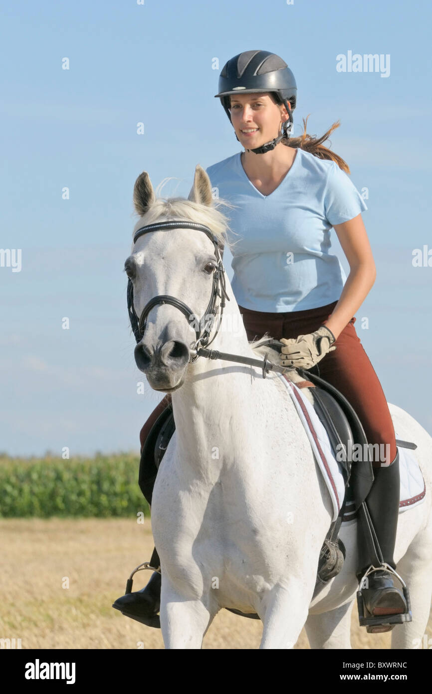Young rider on back of a white German pony galloping in a stubble field ...
