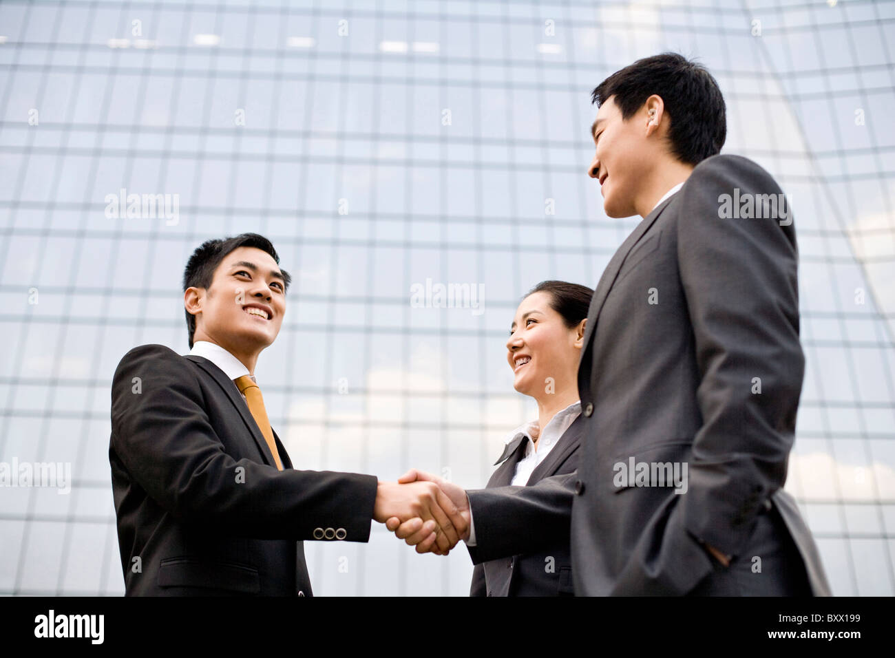 Businessmen shaking hands in front of a tall building Stock Photo - Alamy