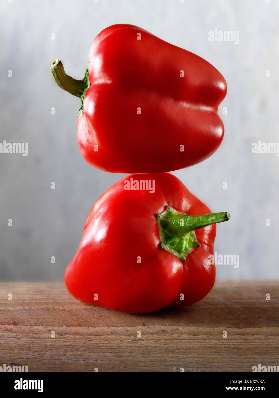 2 red peppers balanced on top of each other against a black background ...