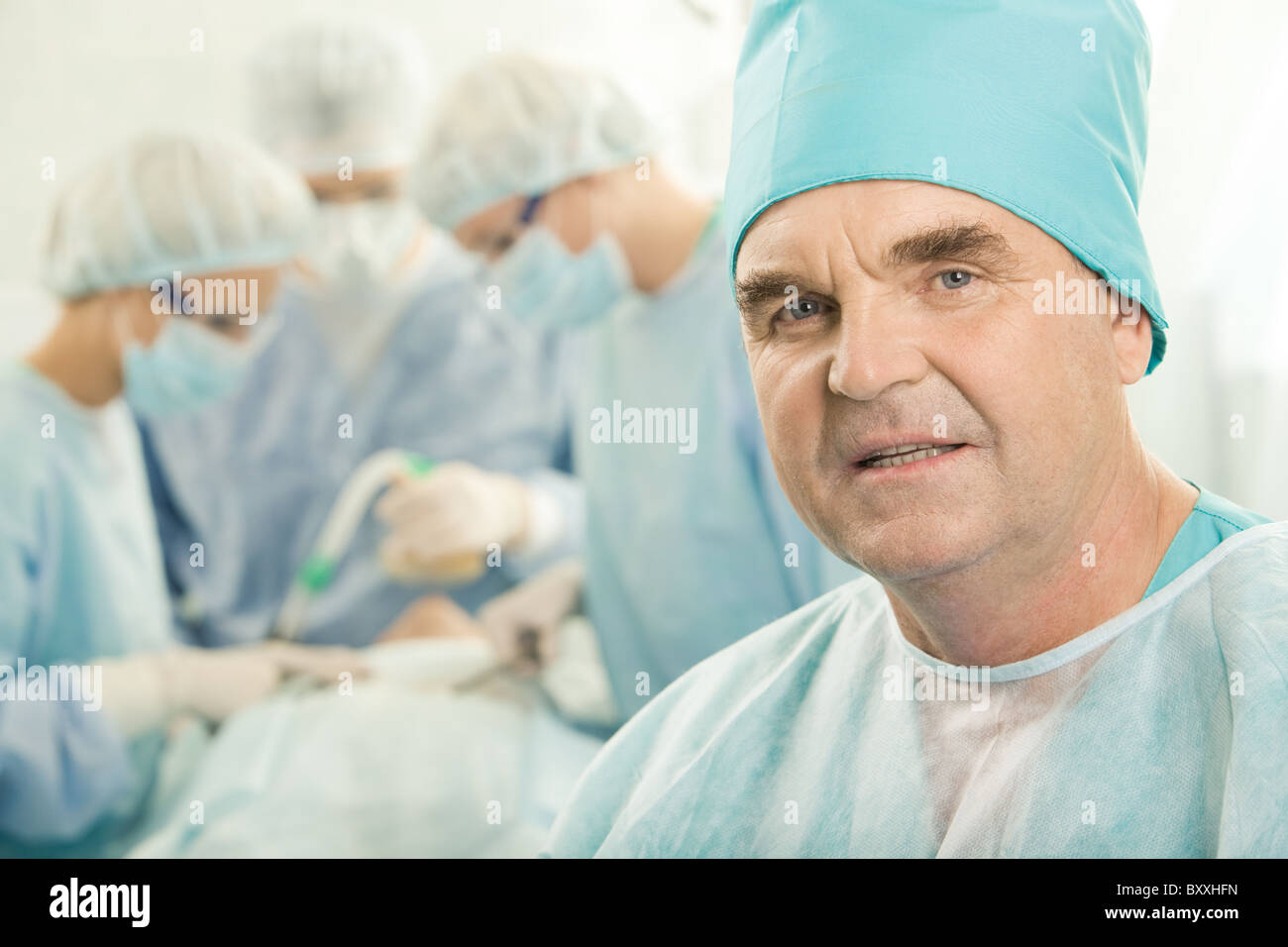 Portrait of confident senior surgeon looking at camera on background of ...
