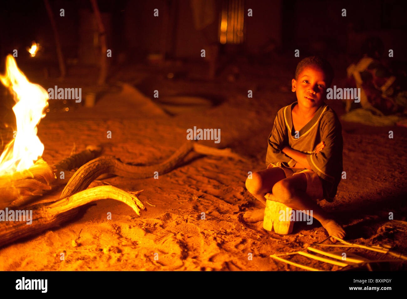 A boy sits next to the Tabaski fire, where a feast grills. Tabaski (Eid ...