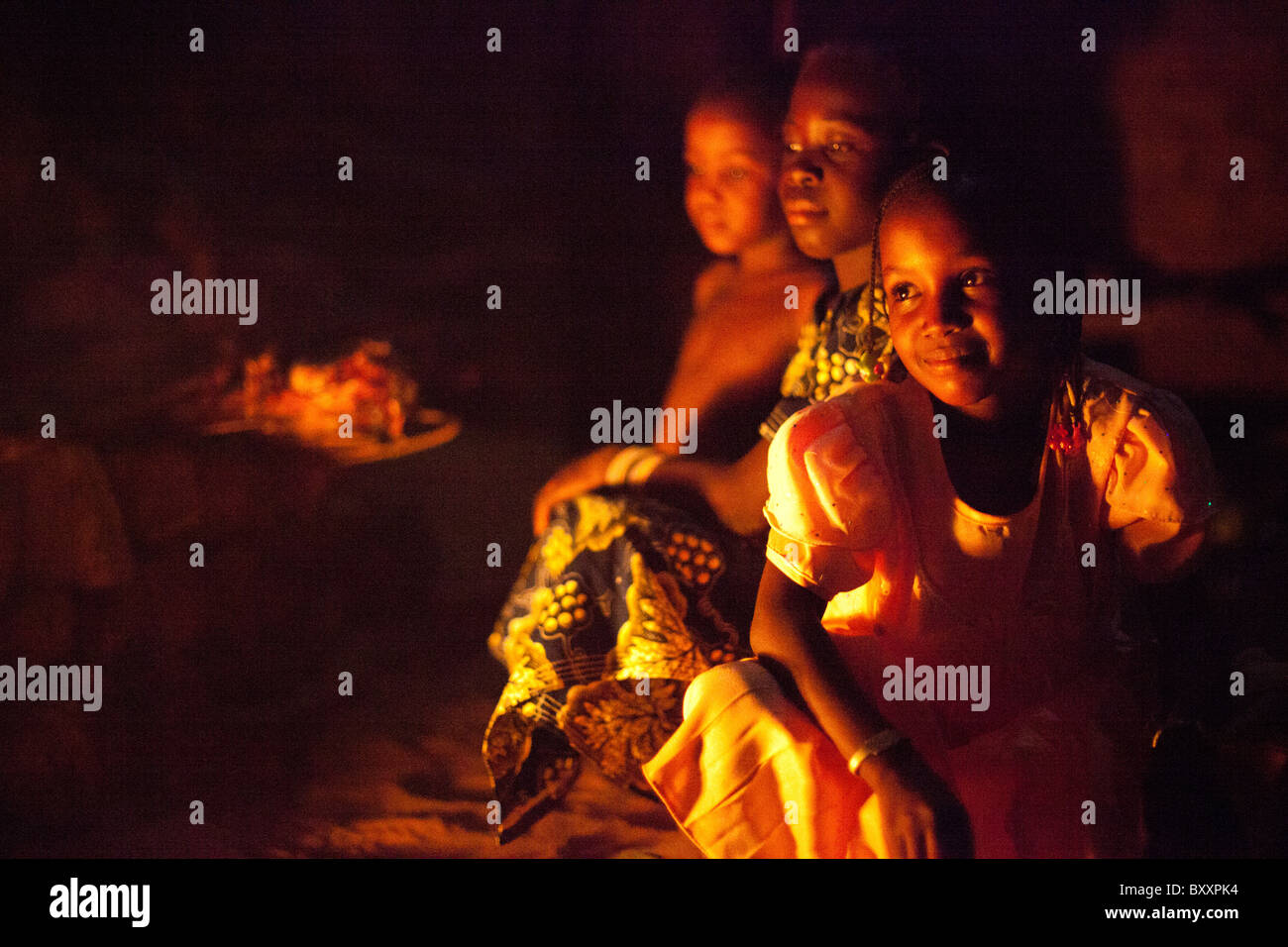 Three girls sit next to the Tabaski fire, where a feast grills. Tabaski ...