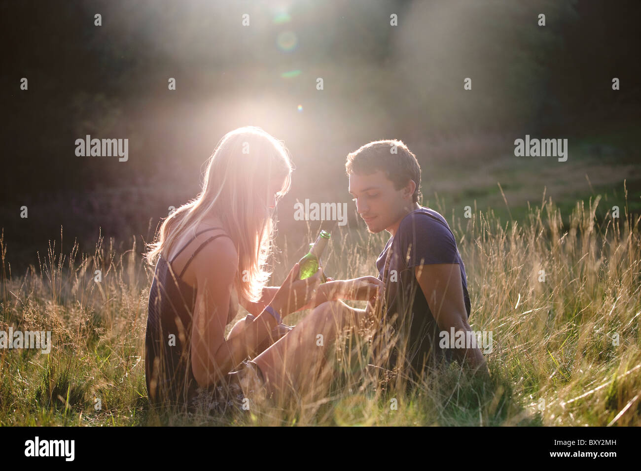 A young couple sitting outdoors in the evening sun, drinking beer Stock ...