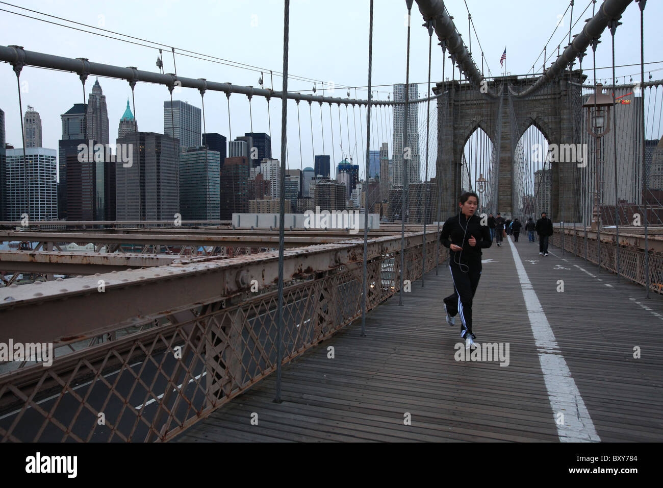 Pedestrians and a runner on Brooklyn bridge walkway with Manhattan in ...