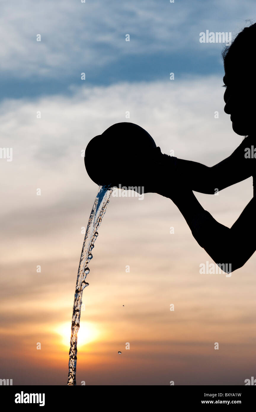 Indian girl pouring water from a pot at sunset. India. Silhouette Stock ...