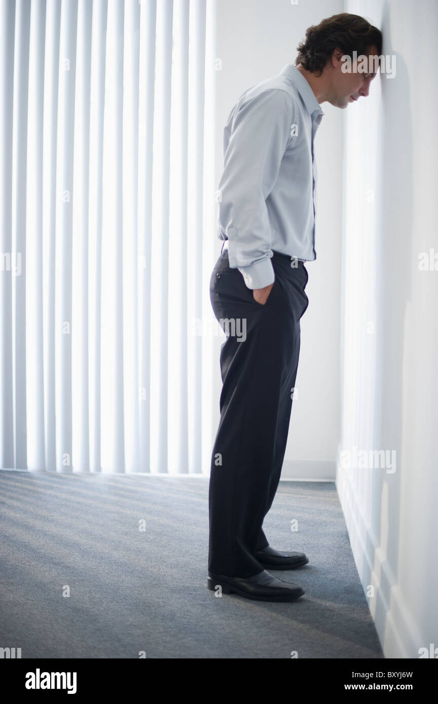 Man in office leaning head against wall Stock Photo - Alamy