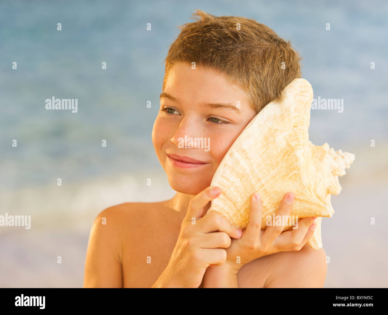 Boy listening to sea shell on beach Stock Photo - Alamy