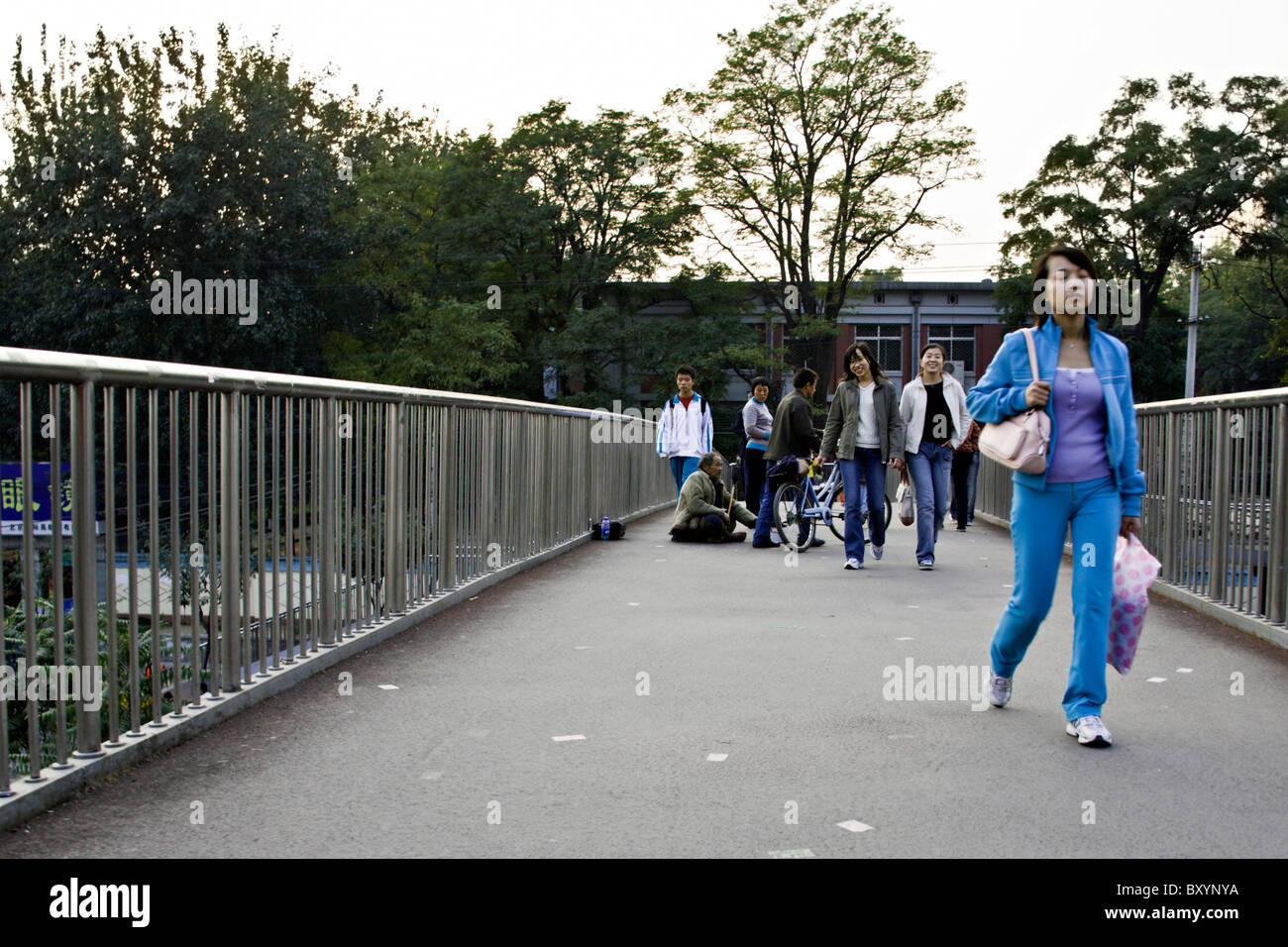 CHINA, BEIJING: Young Chinese teens walk past a beggar sitting on a ...