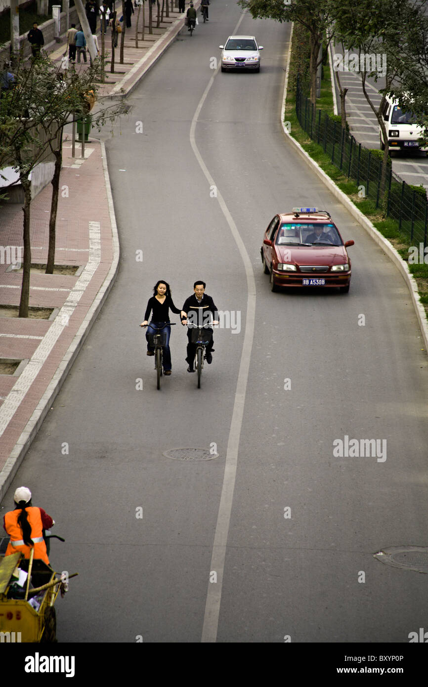 CHINA, BEIJING: Young couple holding hands cycles in the bicycle lane ...