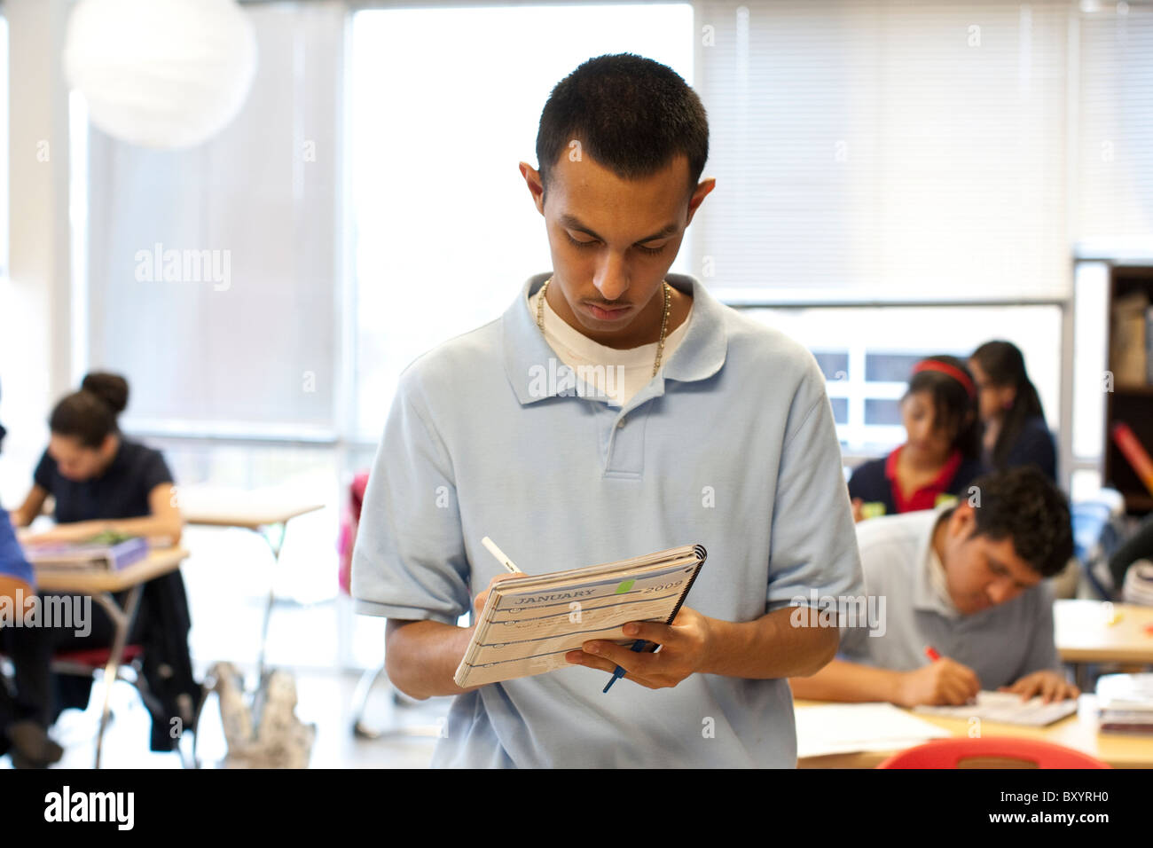 Hispanic male student stands while writing assignment in classroom at ...
