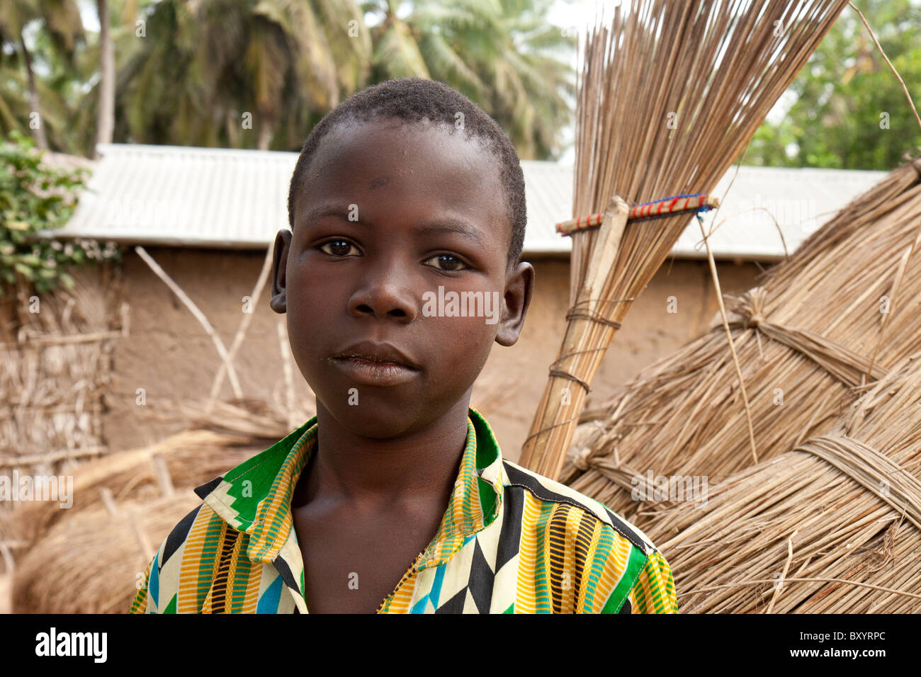 An African boy stands with piles of reeds in the background. His ...