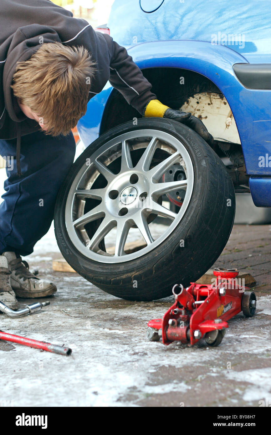 A young Caucasian male mechanic removing a wheel from a car, held up by ...