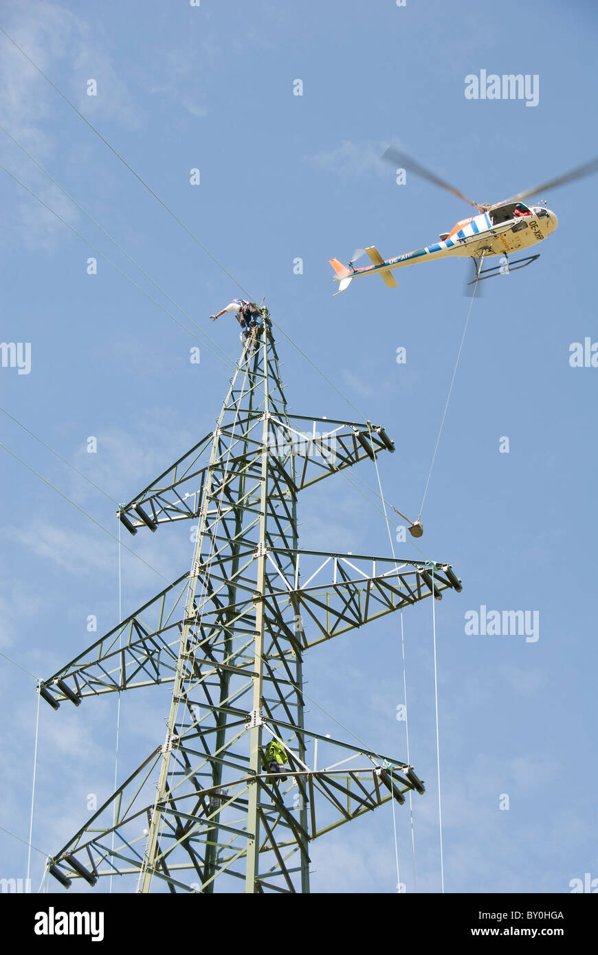 Helicopter connecting power lines, worker on an electricity pylon ...