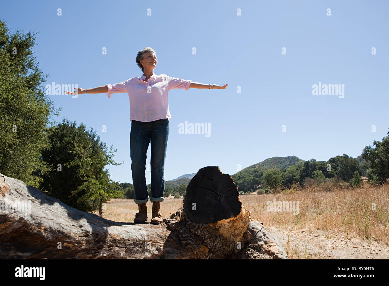 Senior woman standing on a log with open arms Stock Photo - Alamy