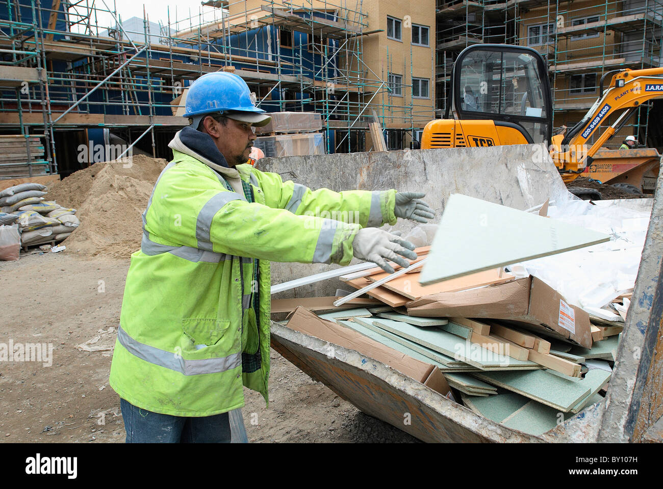 Construction worker loading skip onsite with materials for recycling ...