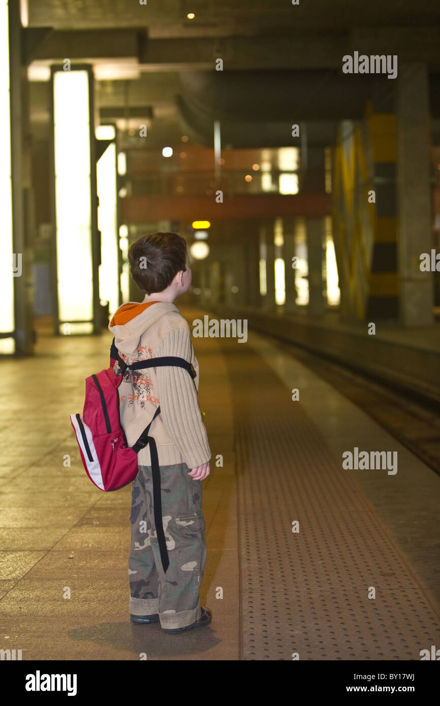 Little boy with a backpack waiting for a train in a railwaystation ...